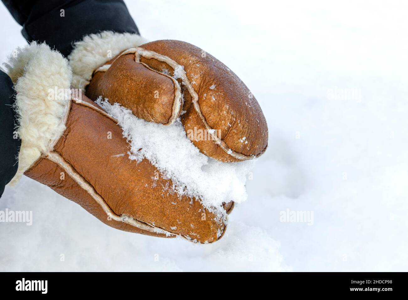 Woman in leather mittens rolls a snowball outdoors, close-up. Hands in ...