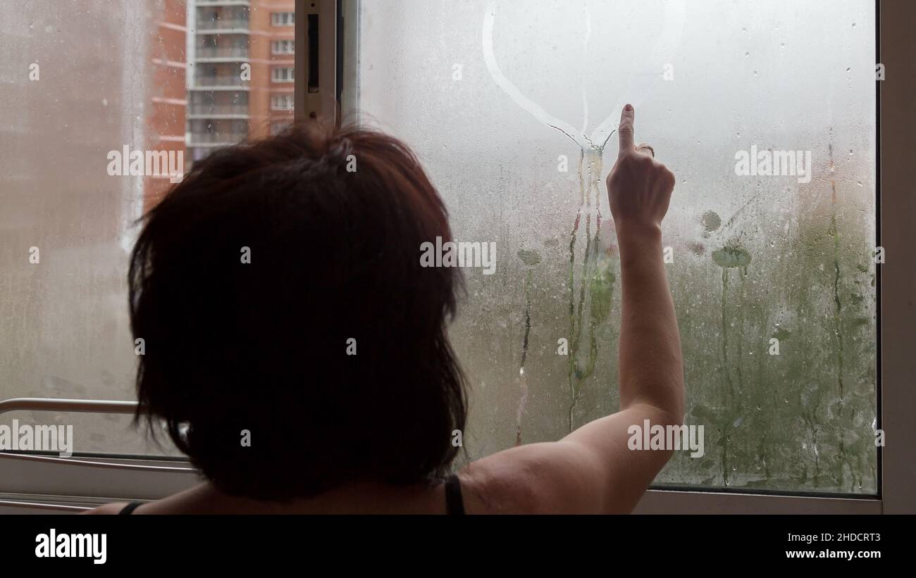 A woman draws a heart with her finger on a wet, fogged window. The ...