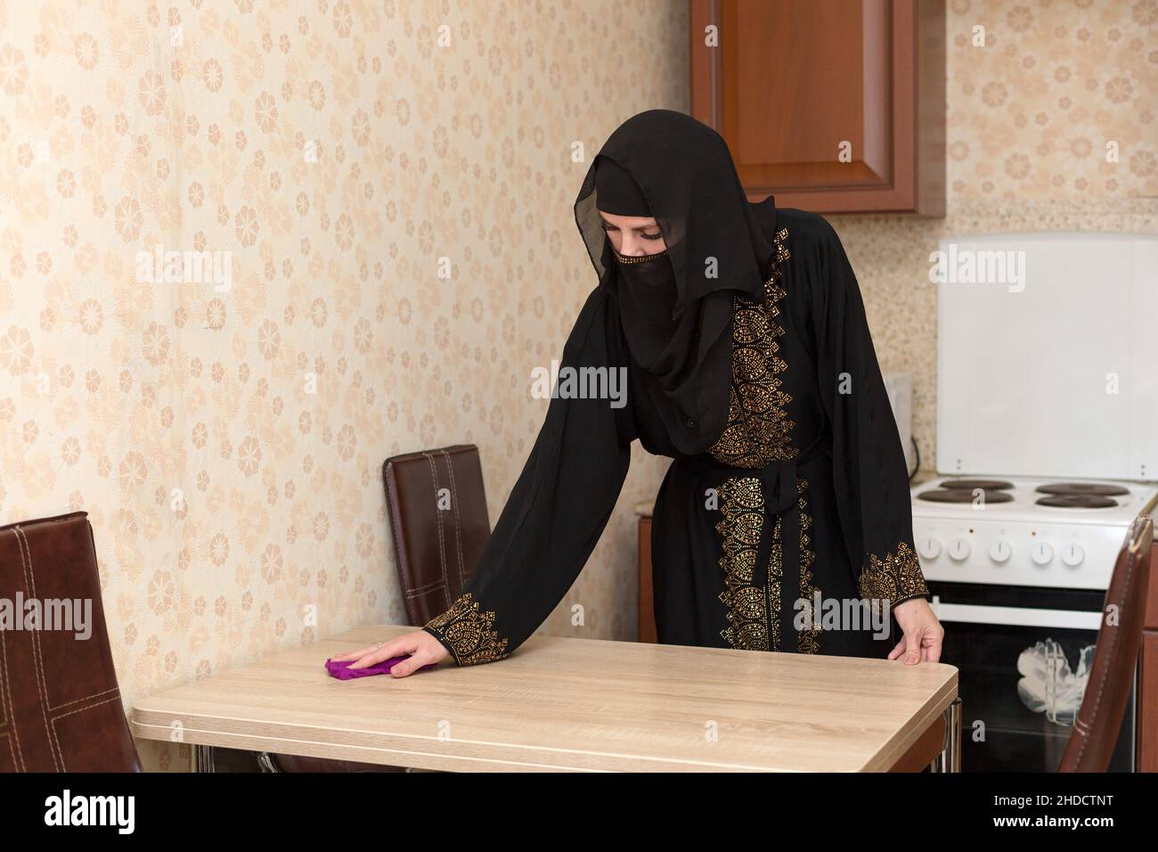 A Muslim woman in national attire cleans the kitchen in the apartment ...