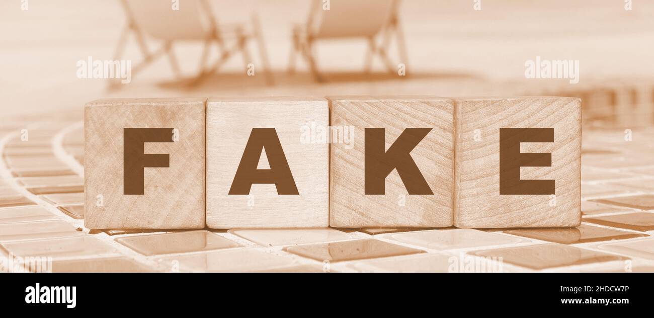 The word FAKE written on wooden cubes on swimming pool border mosaic ...