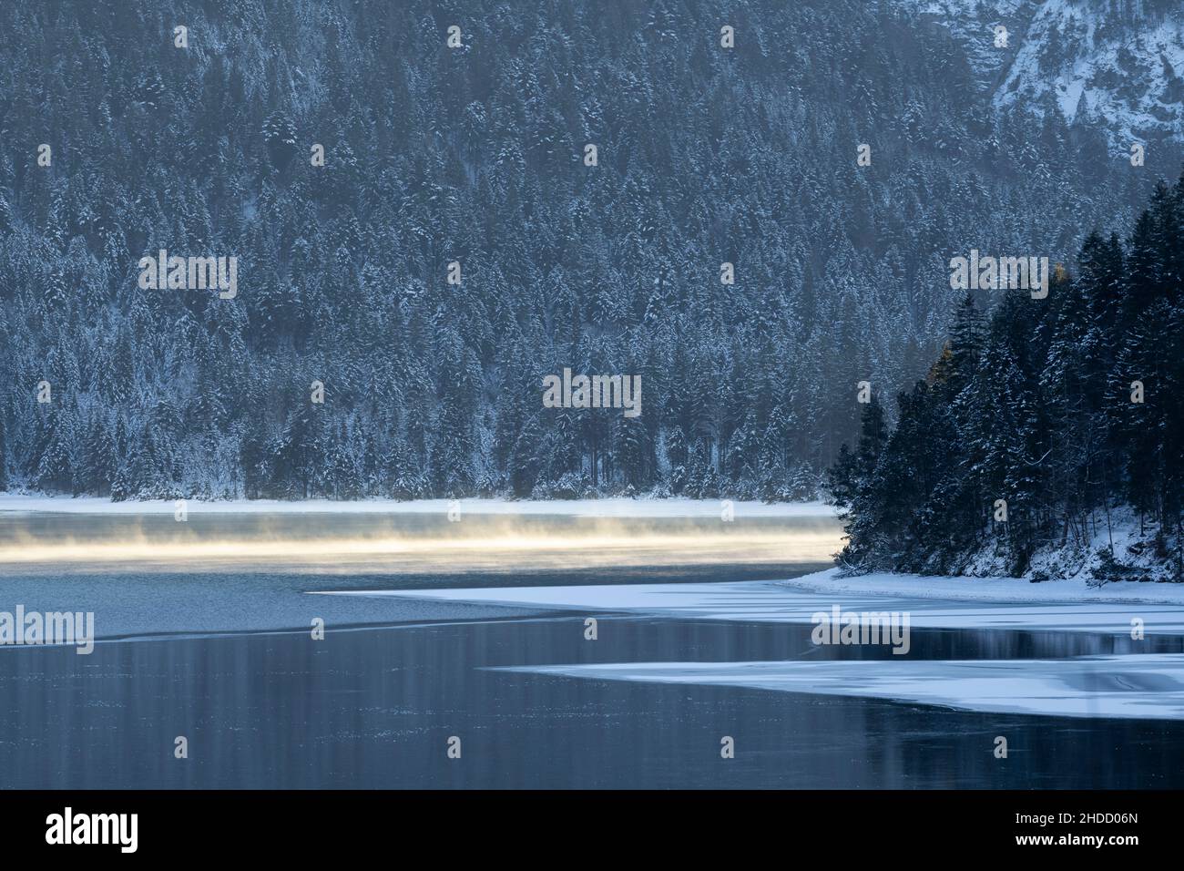 partially frozen lake plansee with water vapor in the sun-heated ice or ...