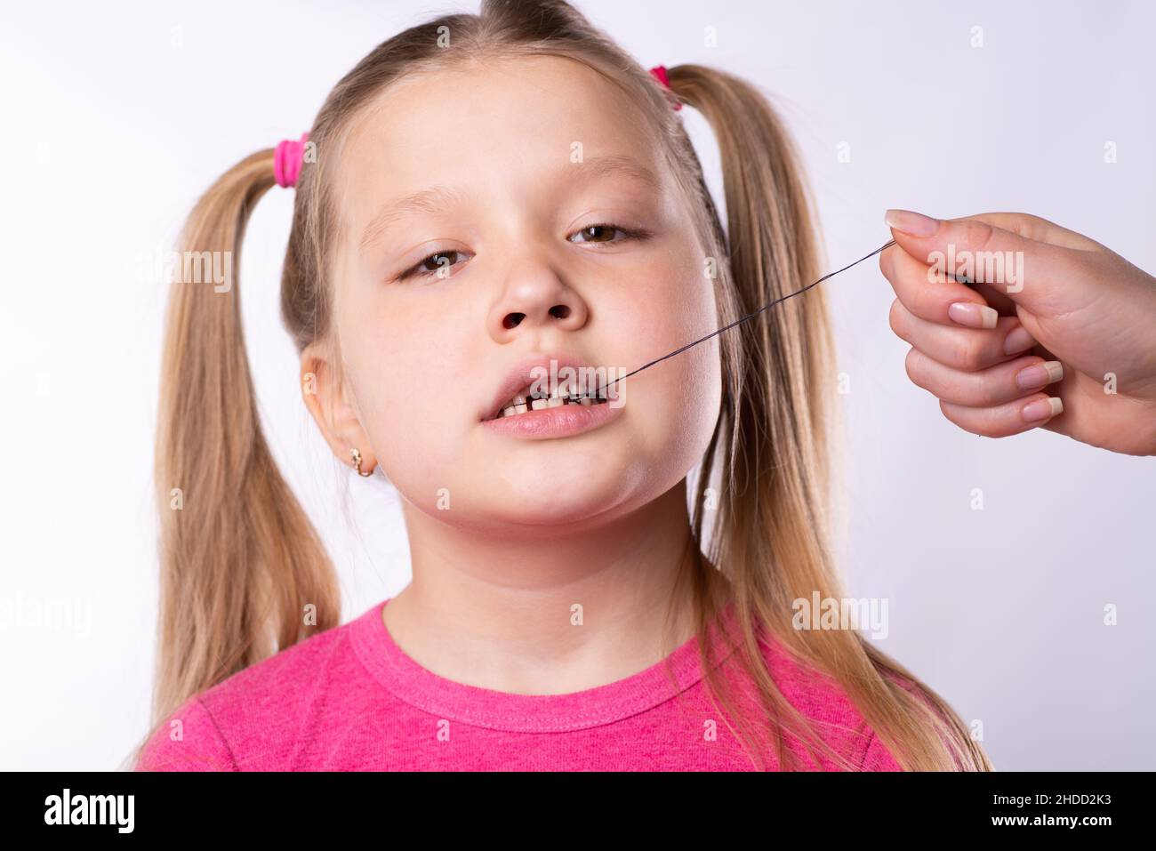 Pulling a milk tooth with a thread from a small beautiful caucasian ...