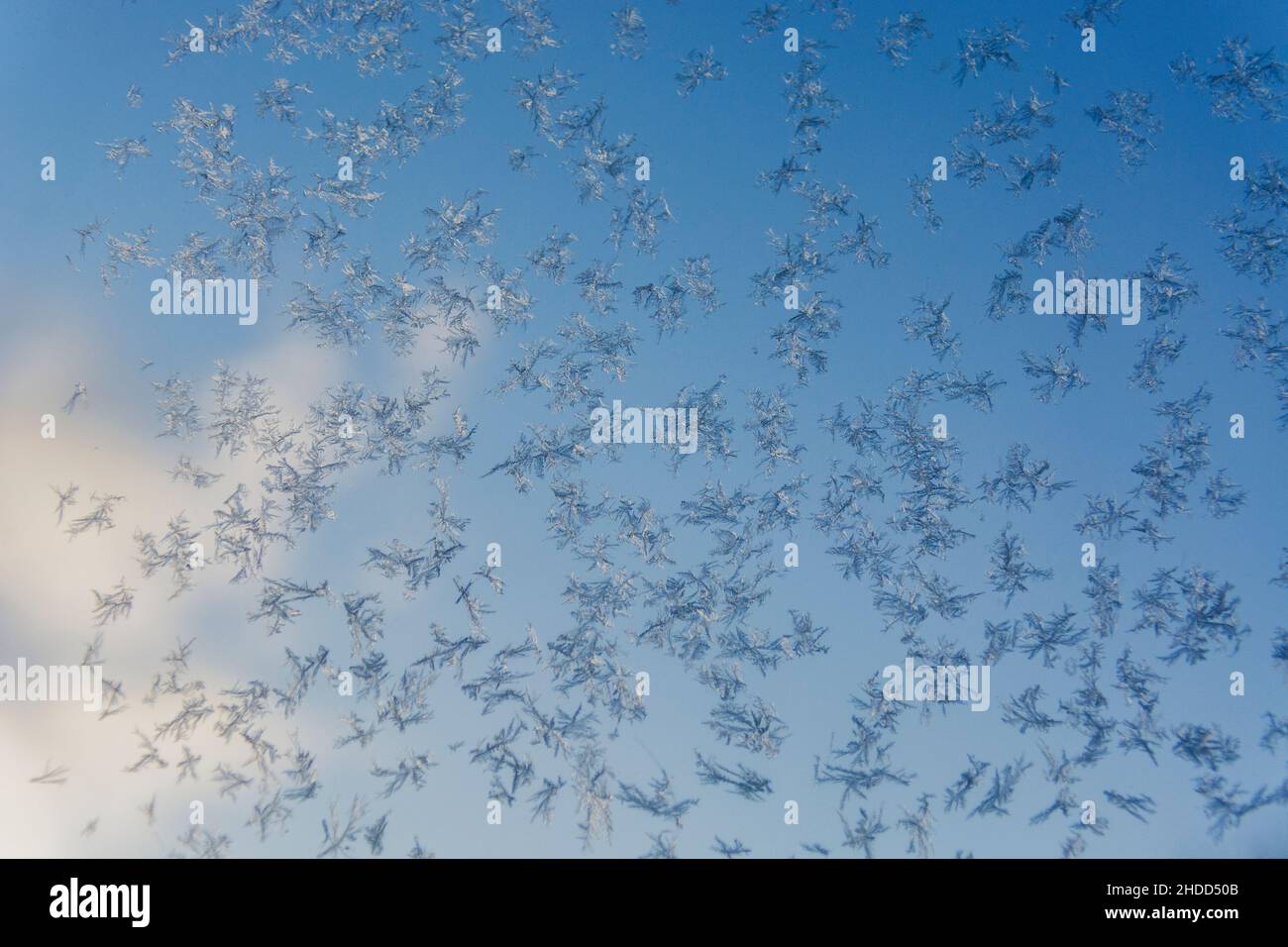 Natural frost pattern on glass window close up with blue winter sky and ...