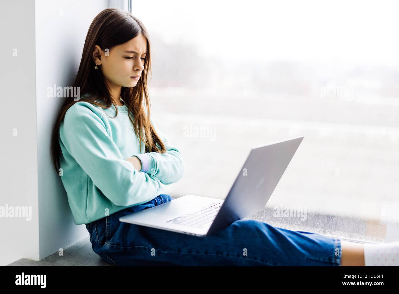 Cute girl sitting on the window sill with laptop studying online at ...