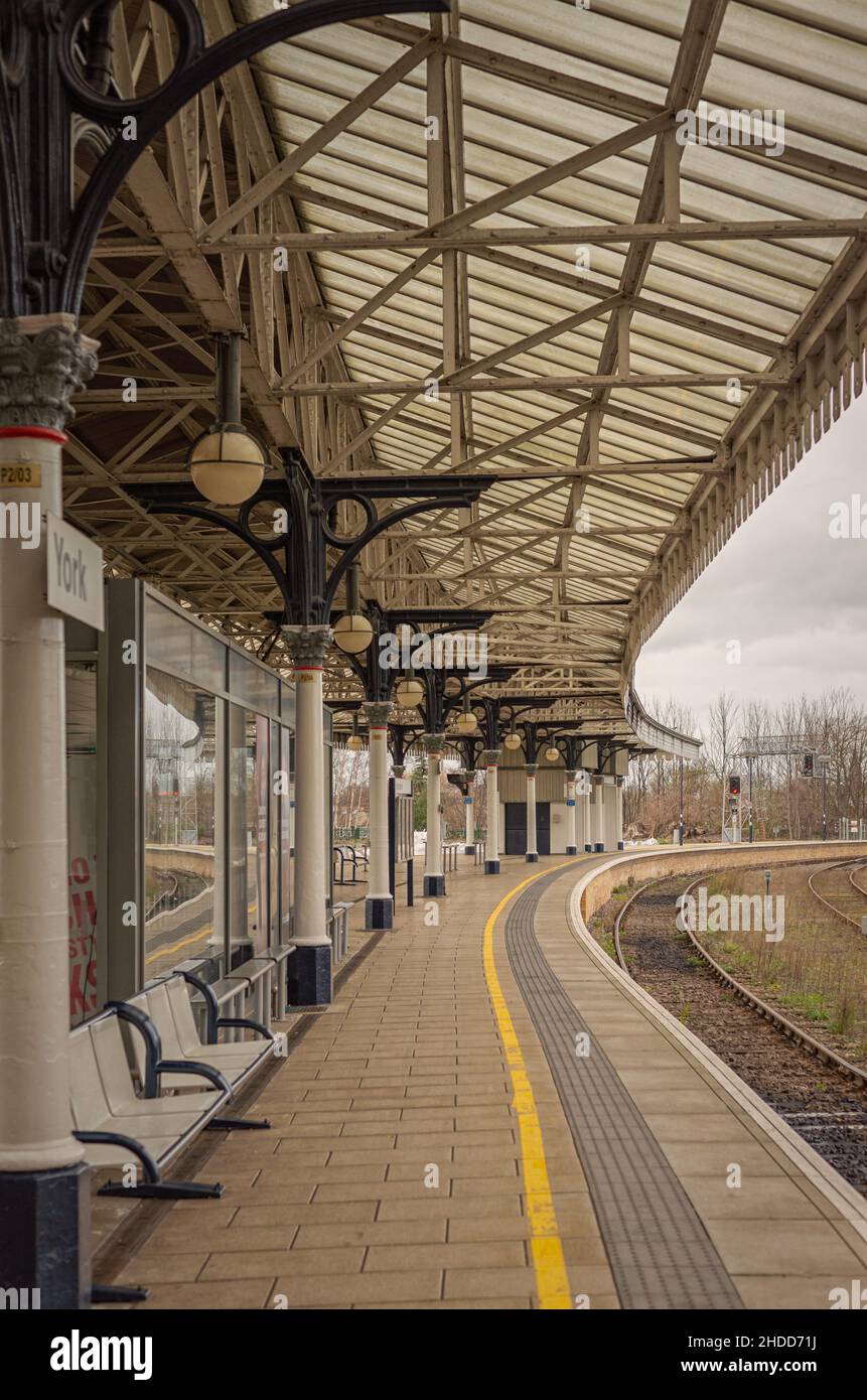 The end of a railway platform and rails curve around a bend. Overhead ...