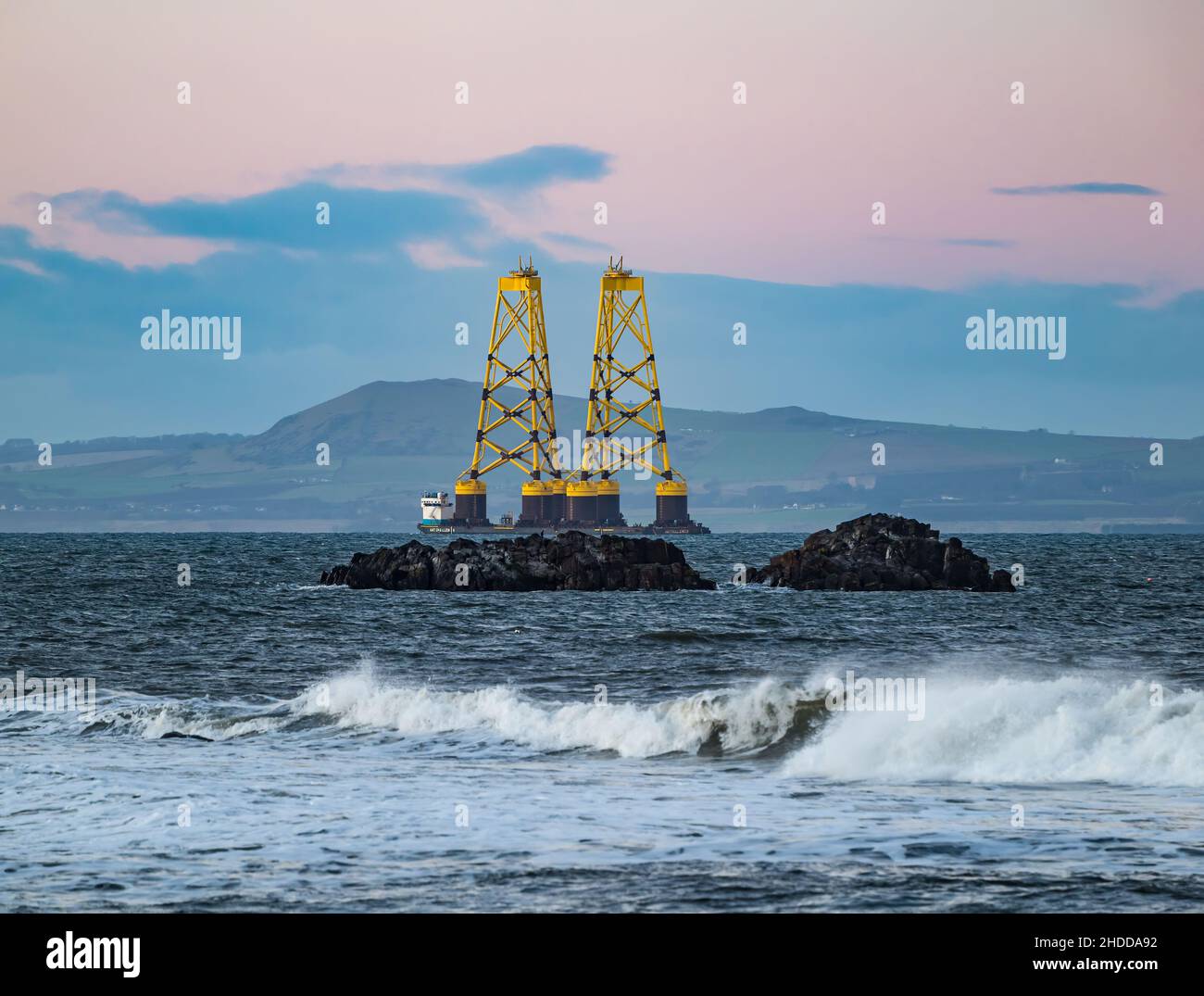 A barge carrying two enormous yellow wind turbine platform heads out to ...