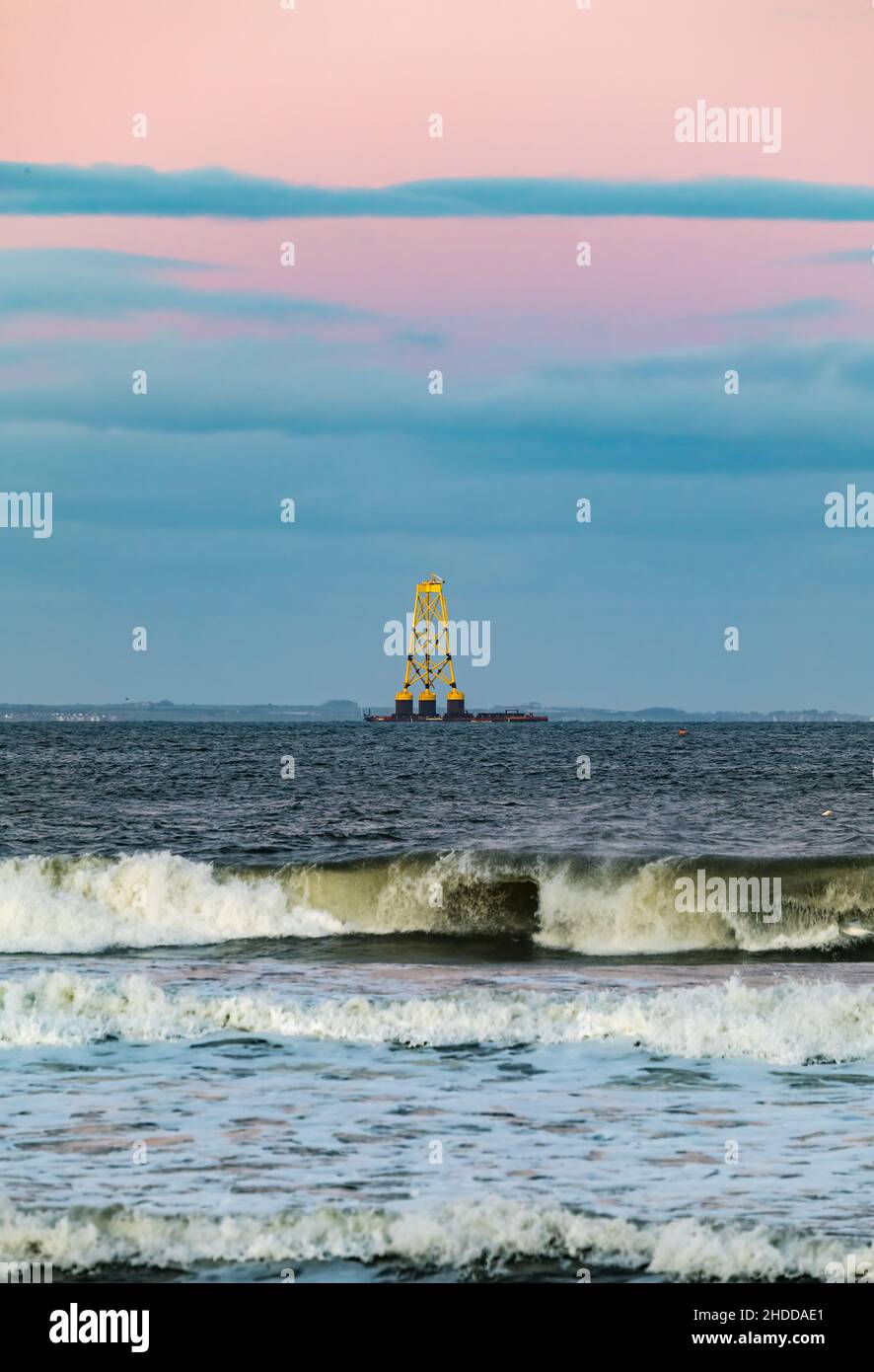 A barge carrying an enormous wind turbine platform heads out to the ...