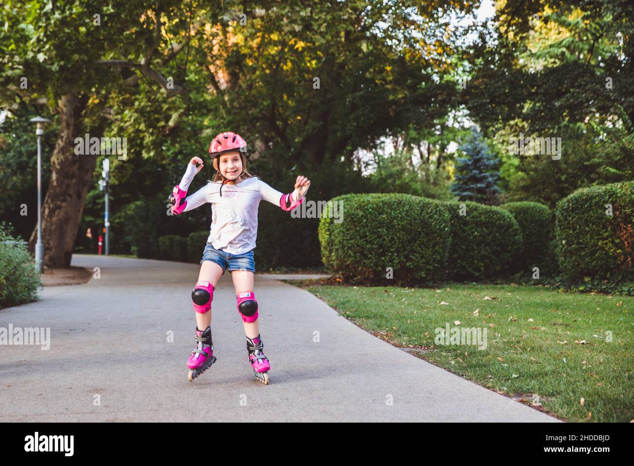 Little girl rides on rollers in summer park. Child wearing protection ...