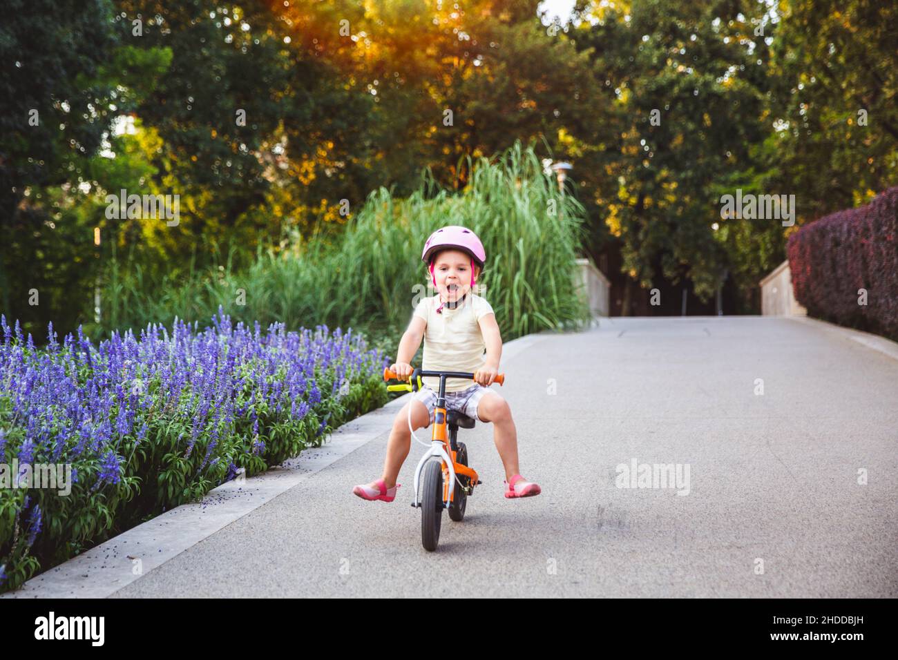Little girl rides on runbike in summer park. Child wearing protection ...