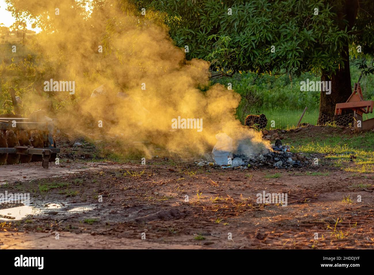 Garbage being burned on a farm generating smoke with golden light ...