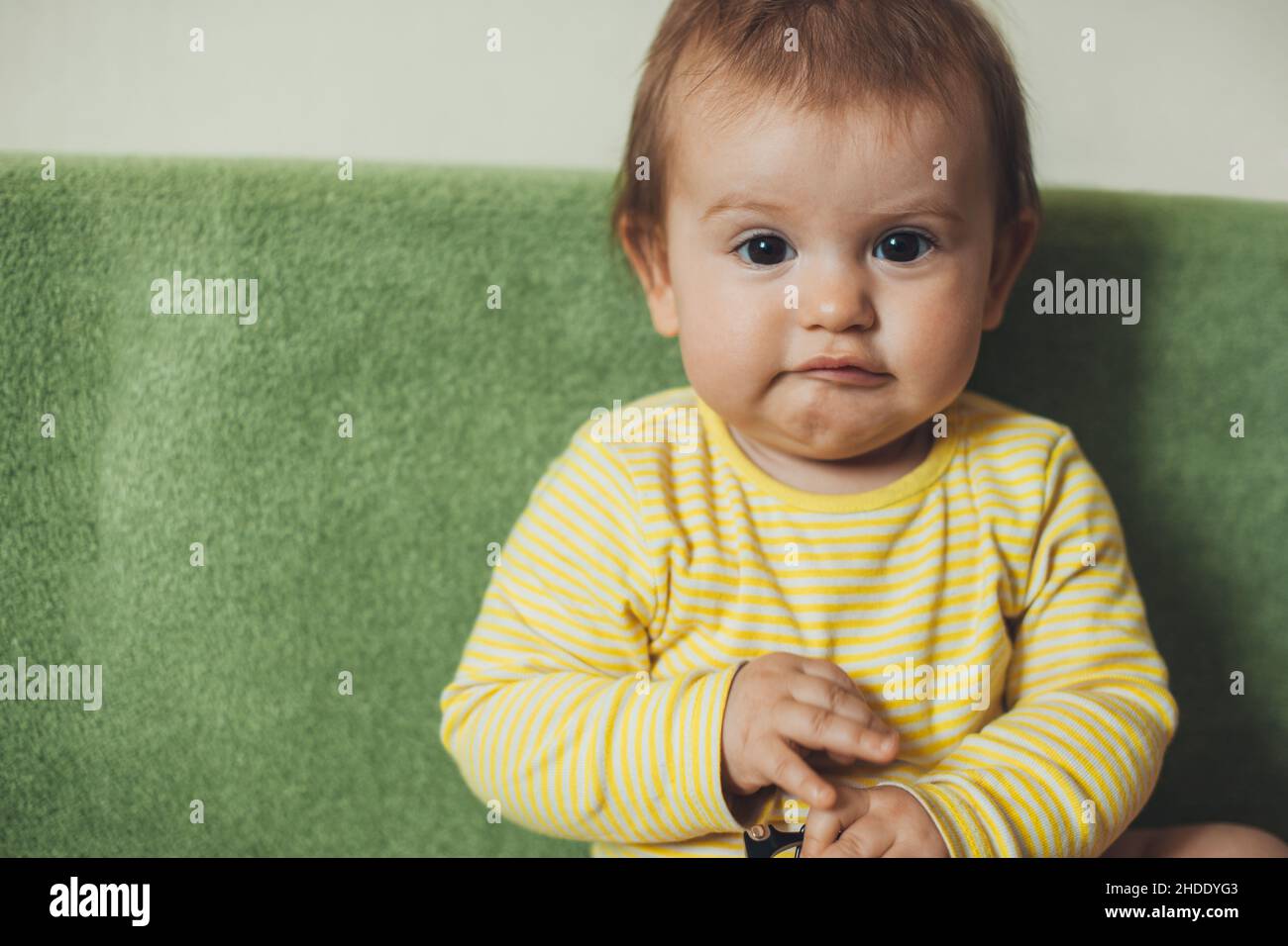 Healthy babygirl sitting on sofa making facial expression. Pretty young ...
