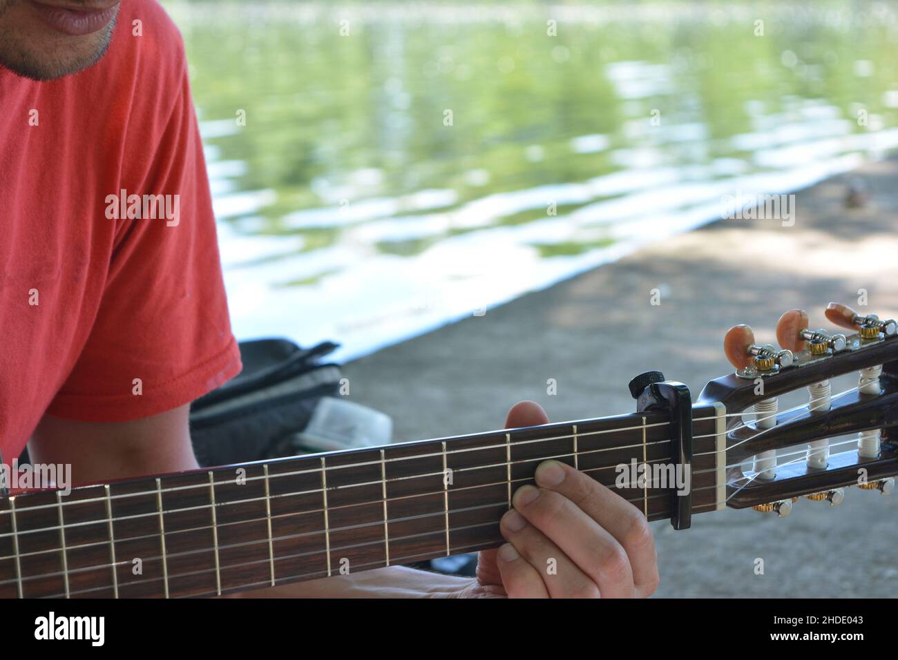 male playing Creole or Spanish guitar with hand and background water ...