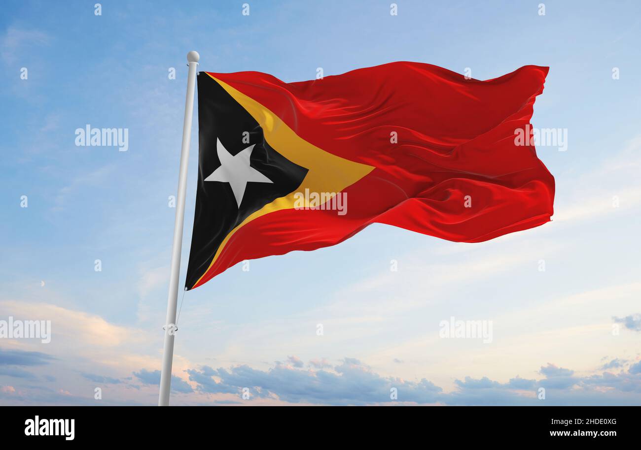 official flag of Timor Leste at cloudy sky background on sunset ...