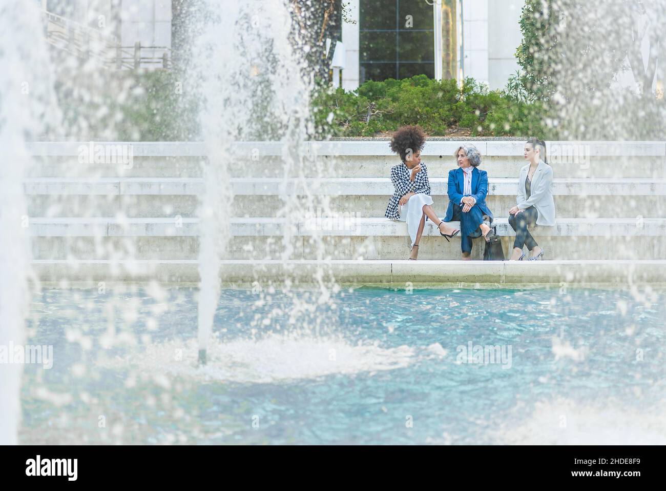 female workers talking while sitting in front of a fountain Stock Photo ...