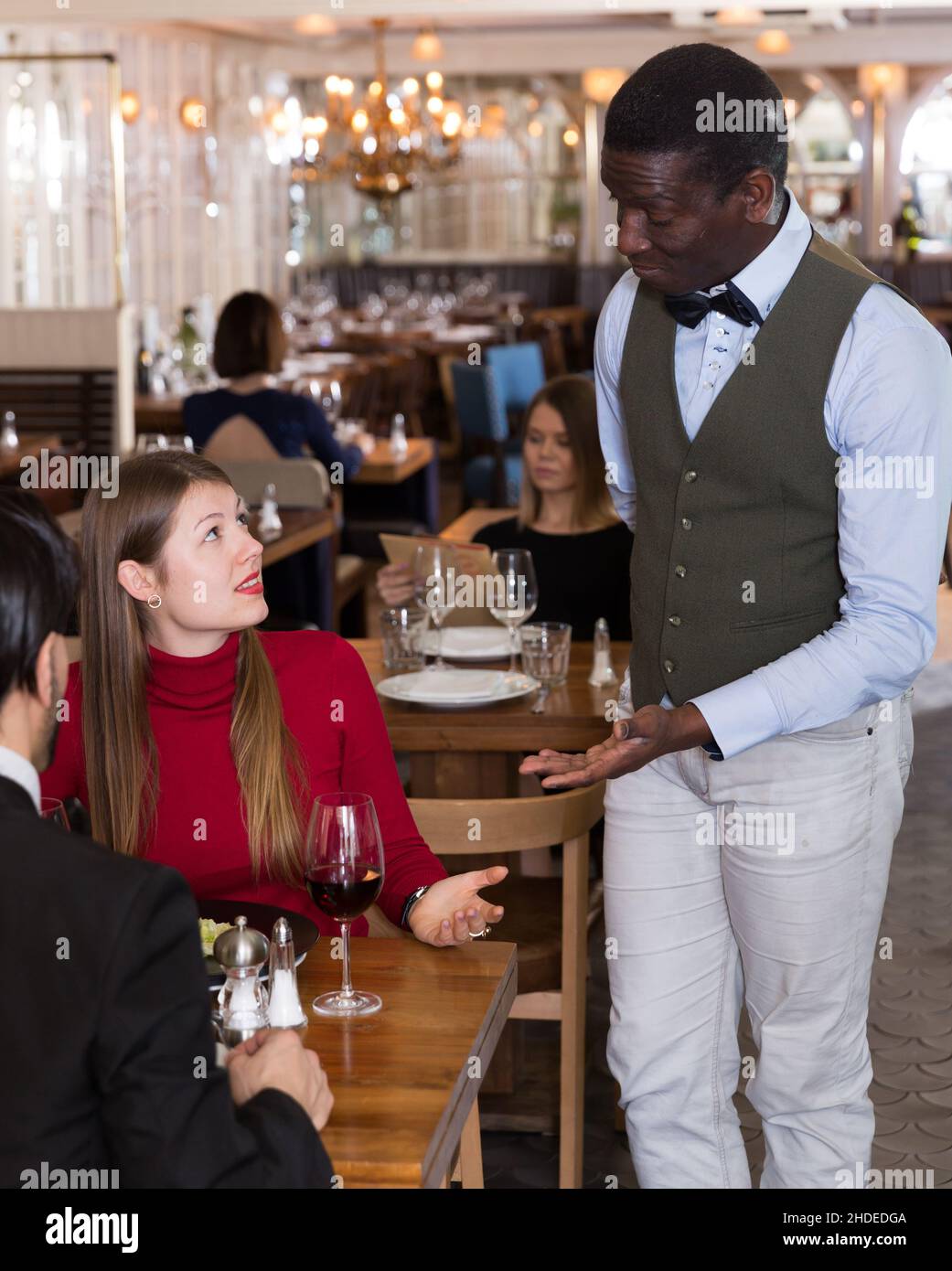 Positive couple talking with African American waiter Stock Photo - Alamy