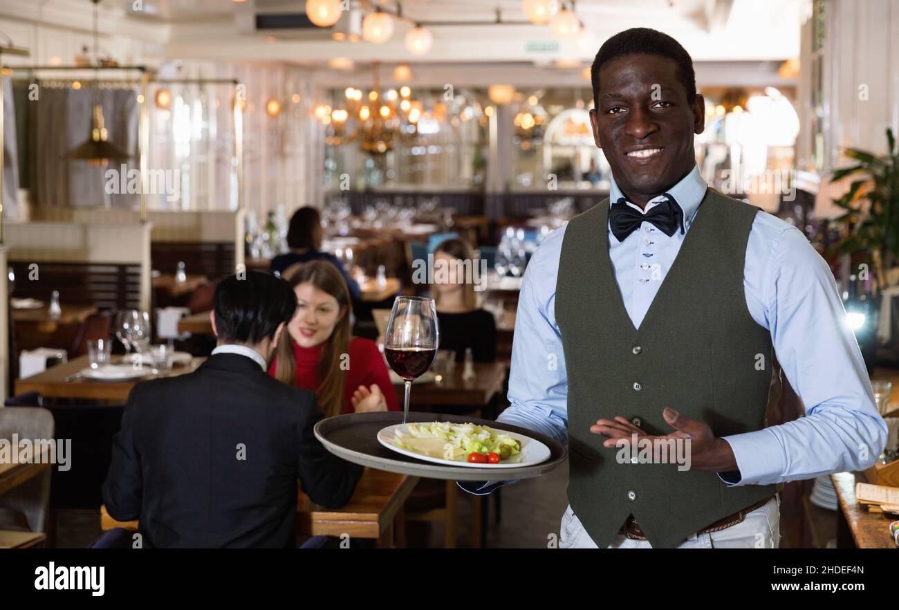 Man waiter is holding tray with order in hall of restaurant Stock Photo ...