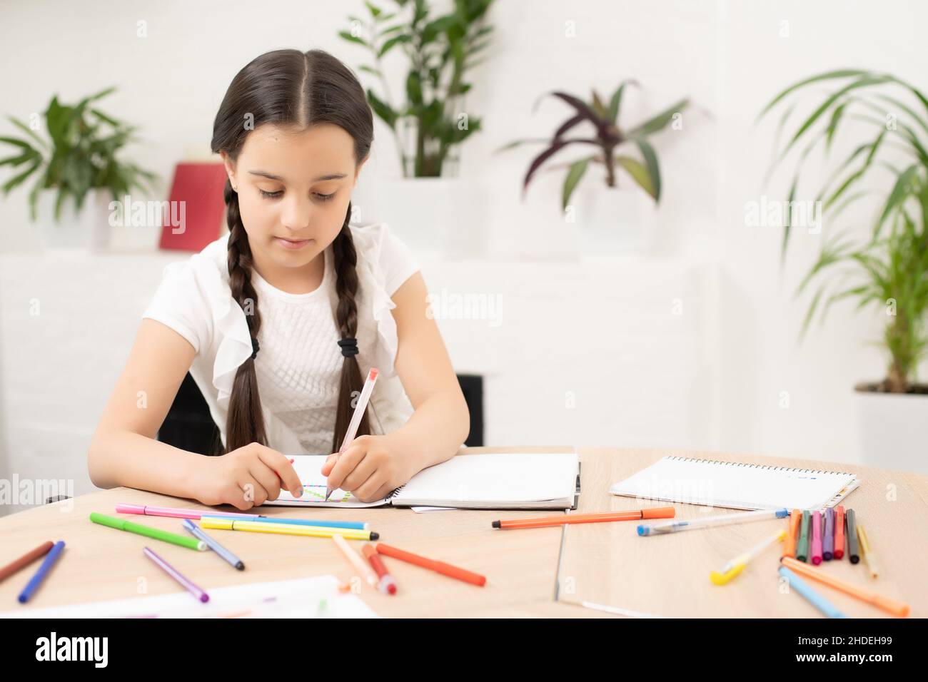 Smart little schoolgirl with pen and books writing a test in a ...