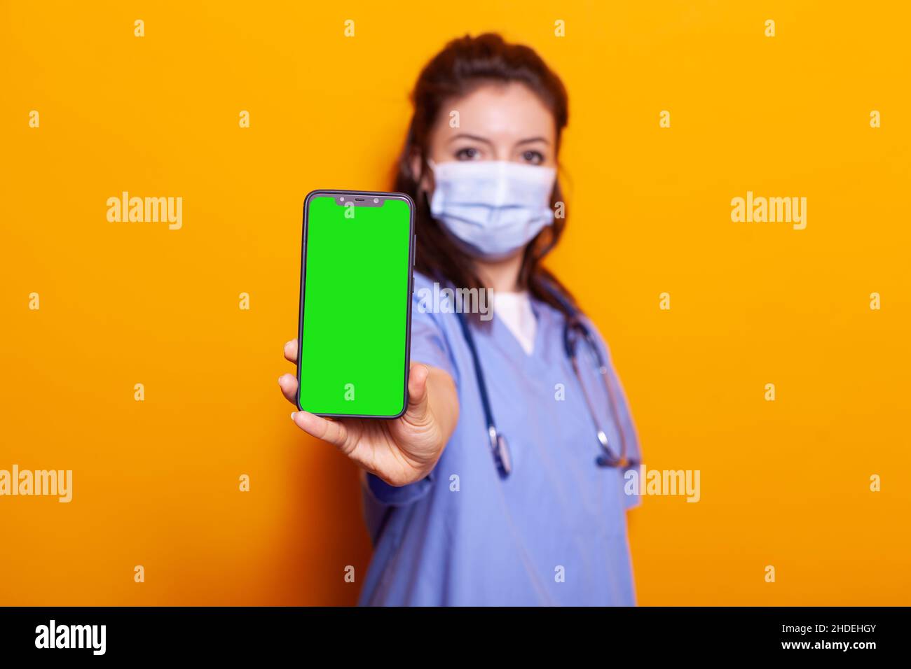 Nurse holding vertical green screen on smartphone while wearing face ...