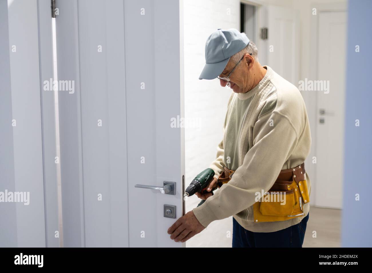 Attractive builder is installing lock in door. He is holding a ...