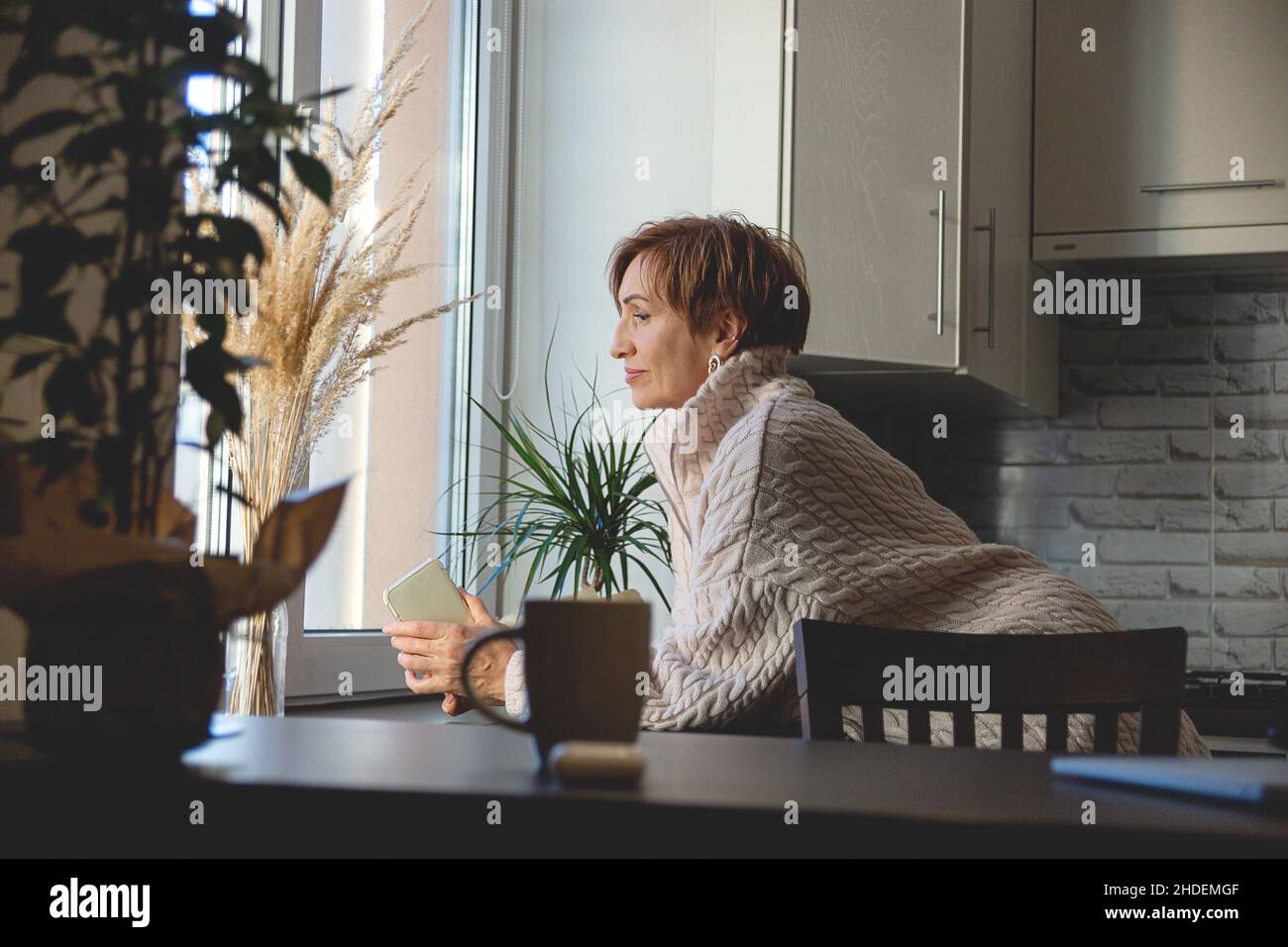 Beautiful middle-aged baby boomer woman in beige sweater holds phone ...