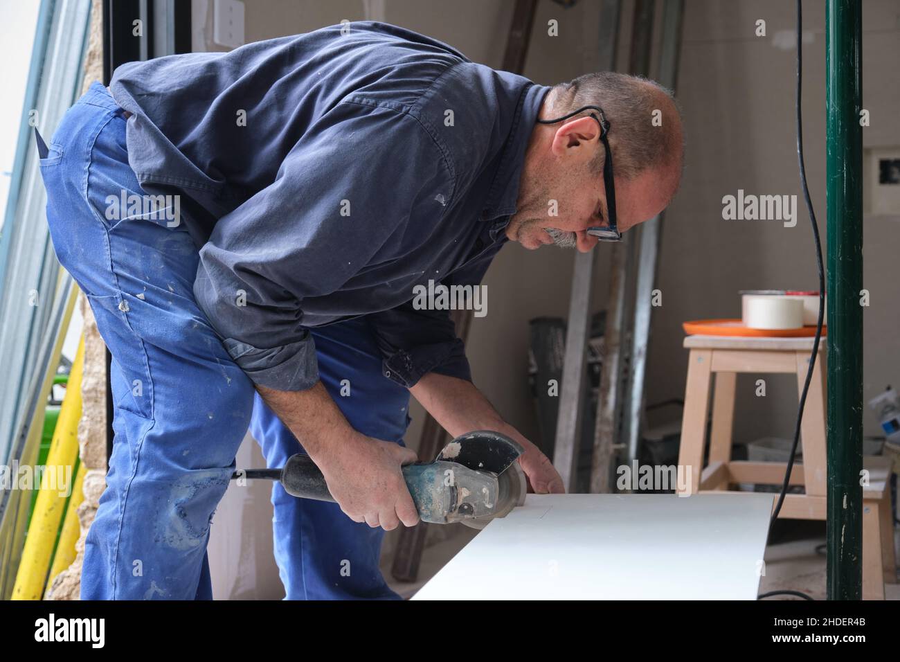 Senior contractor worker cutting a white ceramic tile with a radial saw ...