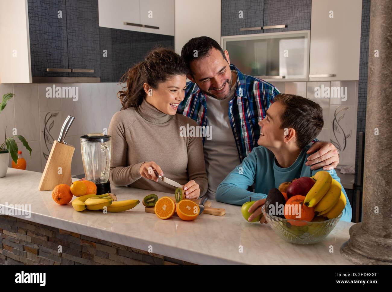 Happy family preparing smoothie drink in kitchen, woman cutting fruits ...