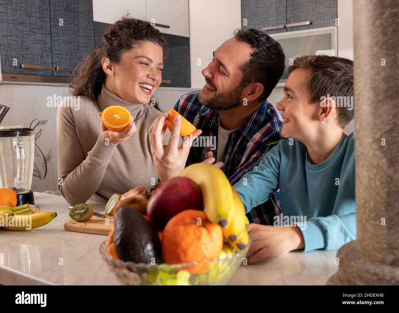 Happy family preparing smoothie drink in kitchen, cutting fruits and ...