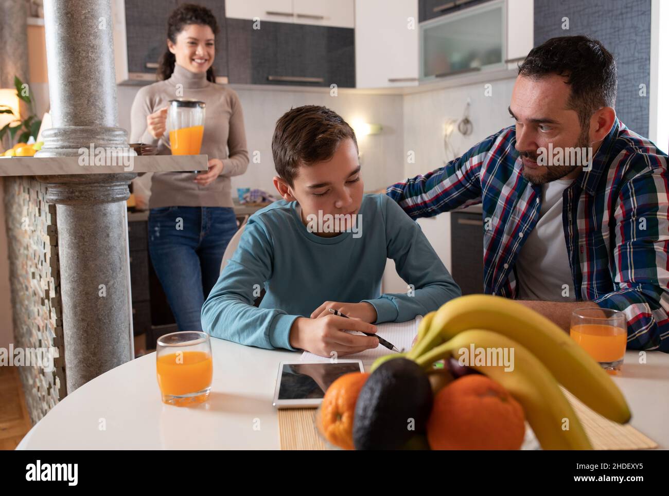 Father and son doing homework at dining table while mother bringing ...