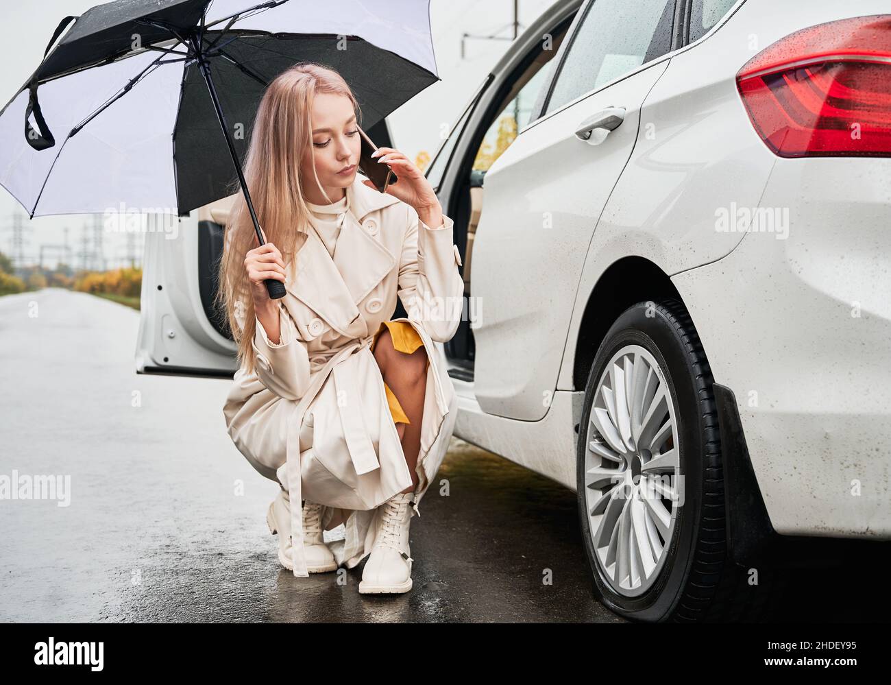 Beautiful woman standing on a road near her white car with punctured ...