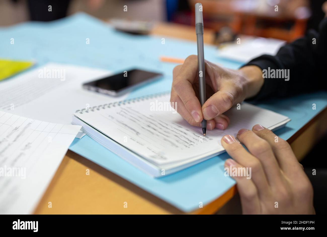 Close up of student's hand writing notes in notebook on desk in ...