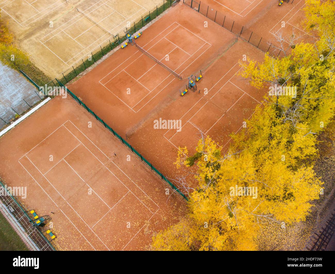 Look down on orange clay tennis courts in city park. Vivid yellow ...