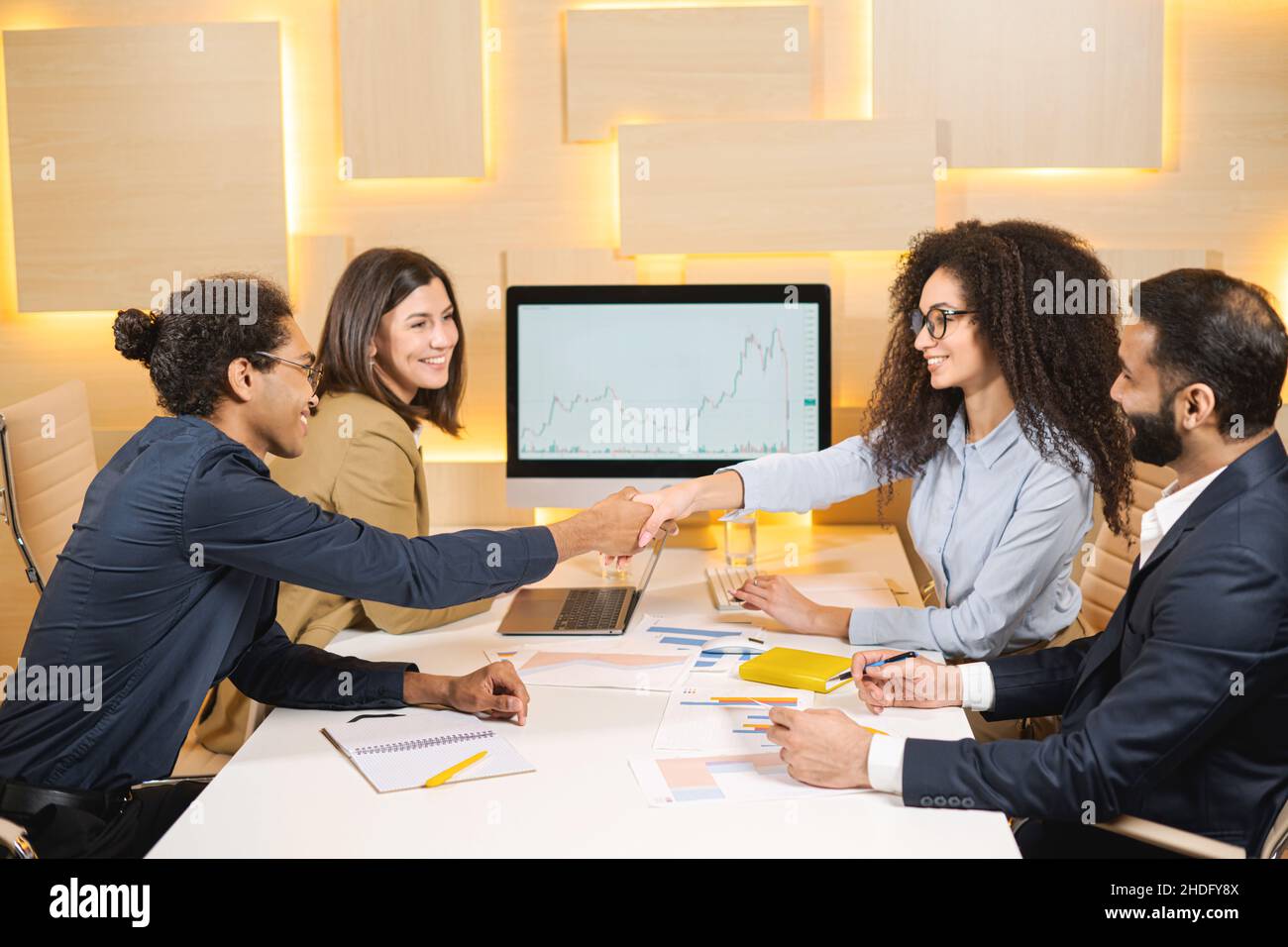 Multiracial team sitting around the table, smiling and putting their ...