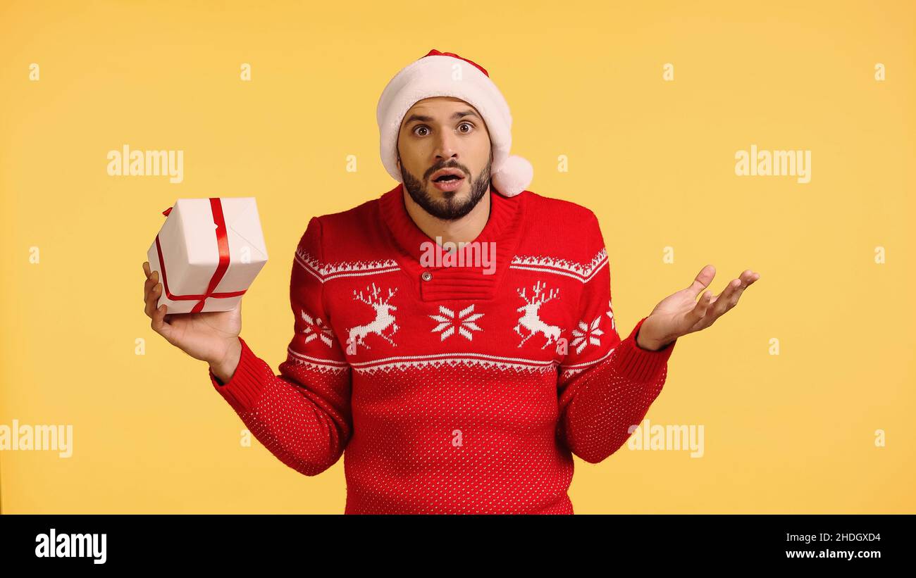 confused man in santa hat holding gift box isolated on yellow Stock ...
