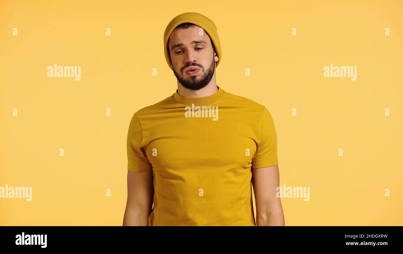 tired young man in beanie hat and t-shirt puffing cheeks isolated on yellow Stock Photo - Alamy