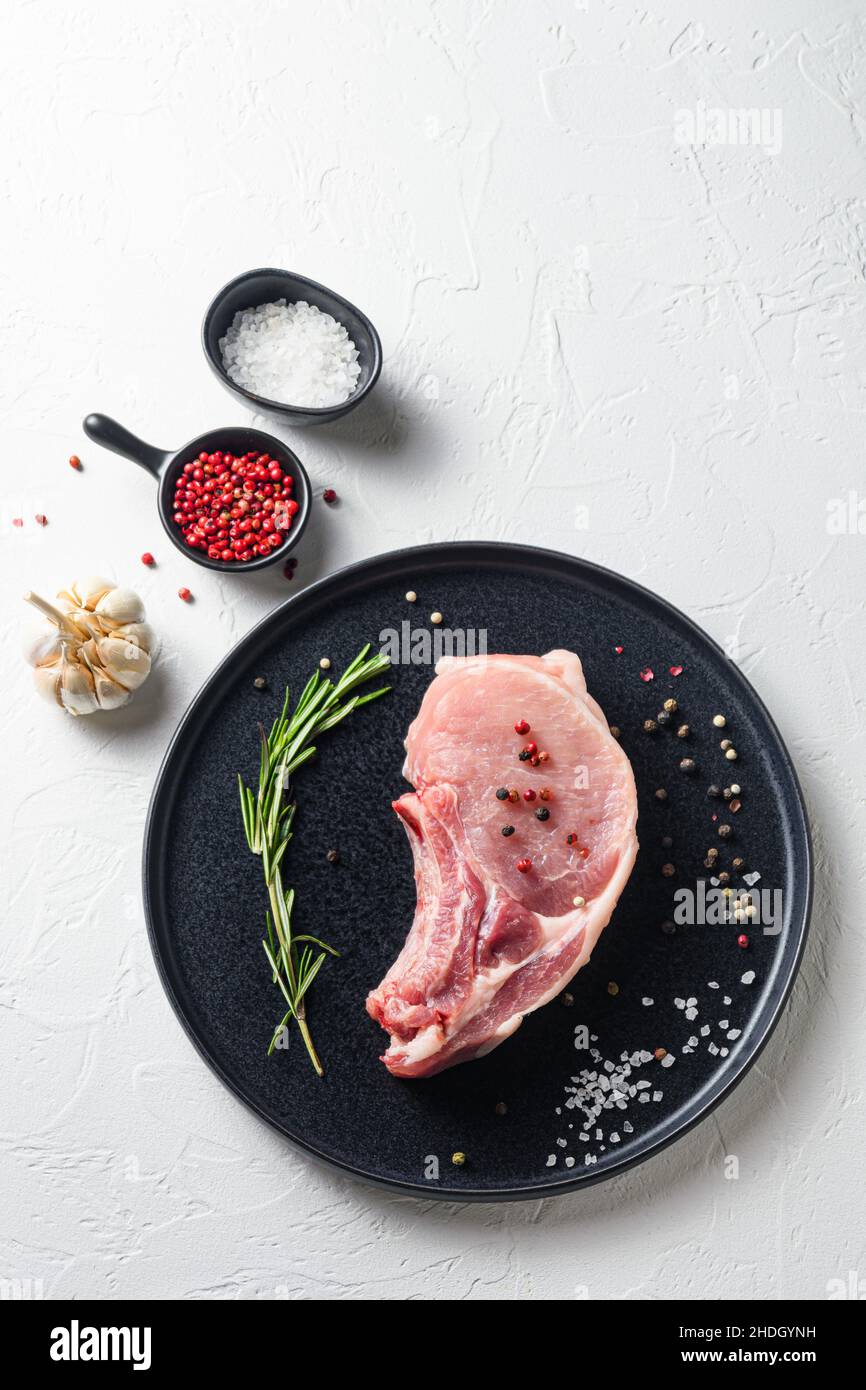 Raw Pork Loin chops in a black round plate on a white stone background ...
