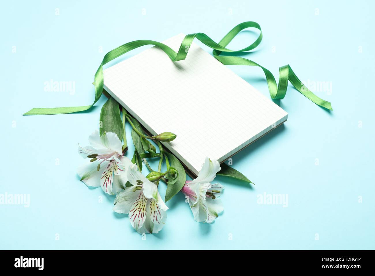 Lilies, green ribbon and blank notebook on blue background Stock Photo ...