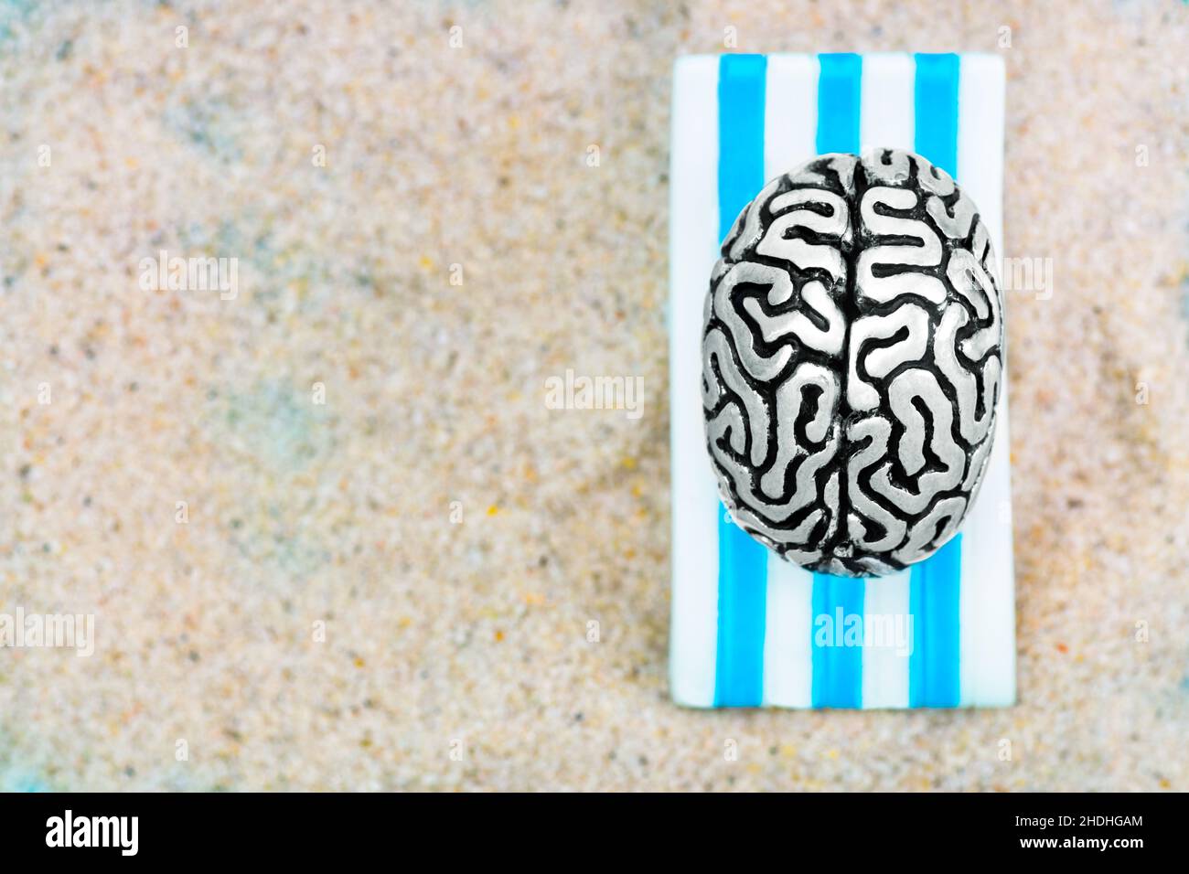 Top view of a human brain lying on a sunbed on a sandy beach. Mind ...