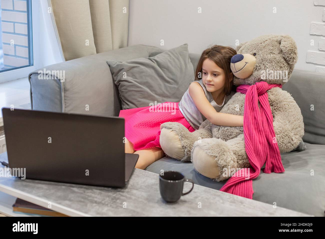 Child girl watching laptop screen, hugging teddy bear. Concept of ...