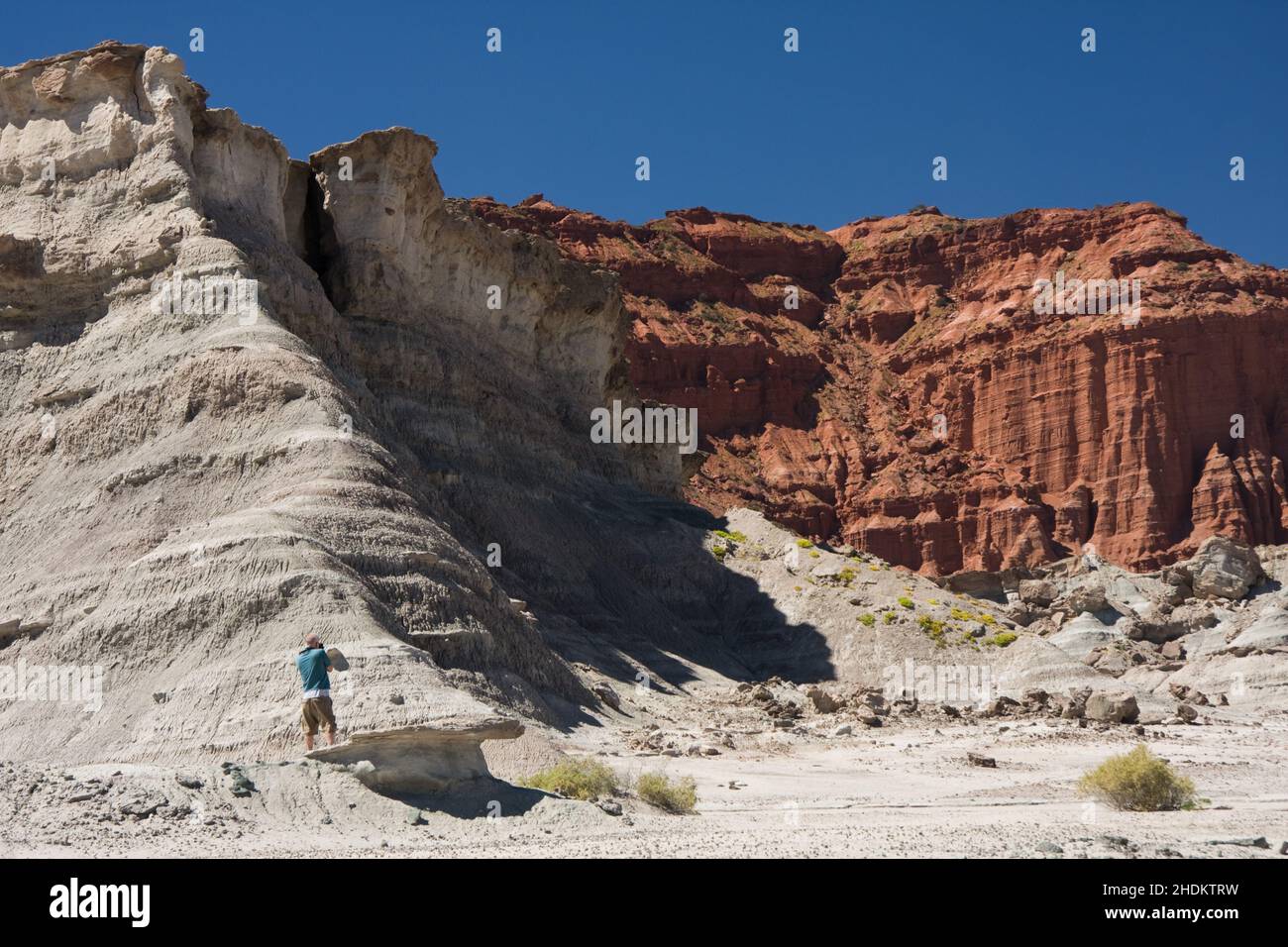 Shot of chipped rock wall in a desert with human standing on a slope ...