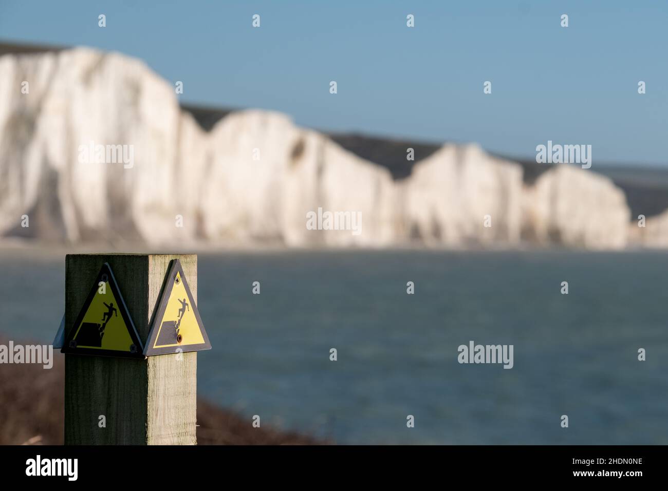 Yellow and black sign warning of the danger of erosion at the cliff ...