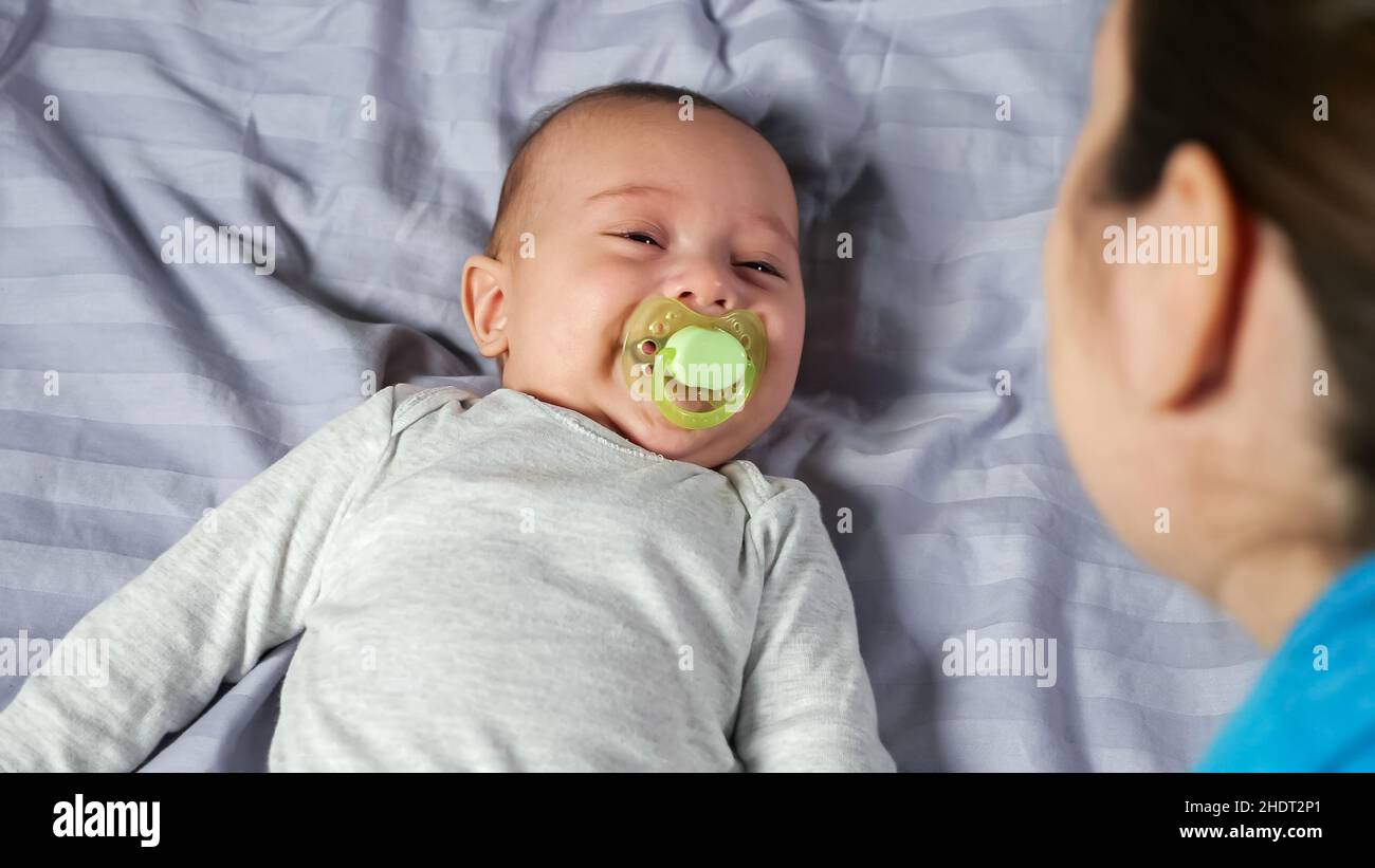 Young mother plays with baby boy making son with dummy smile Stock ...