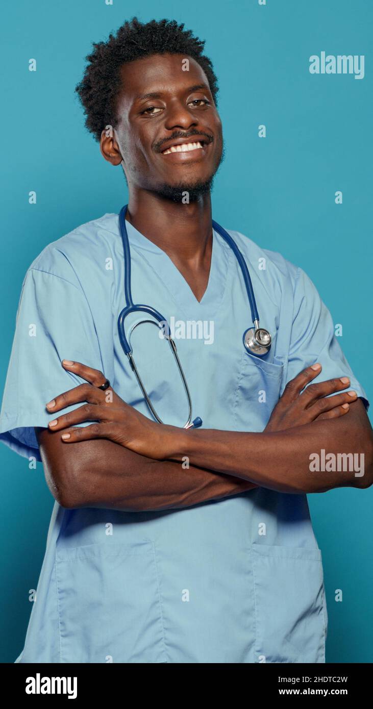 Positive nurse standing with crossed arms and smiling in studio ...