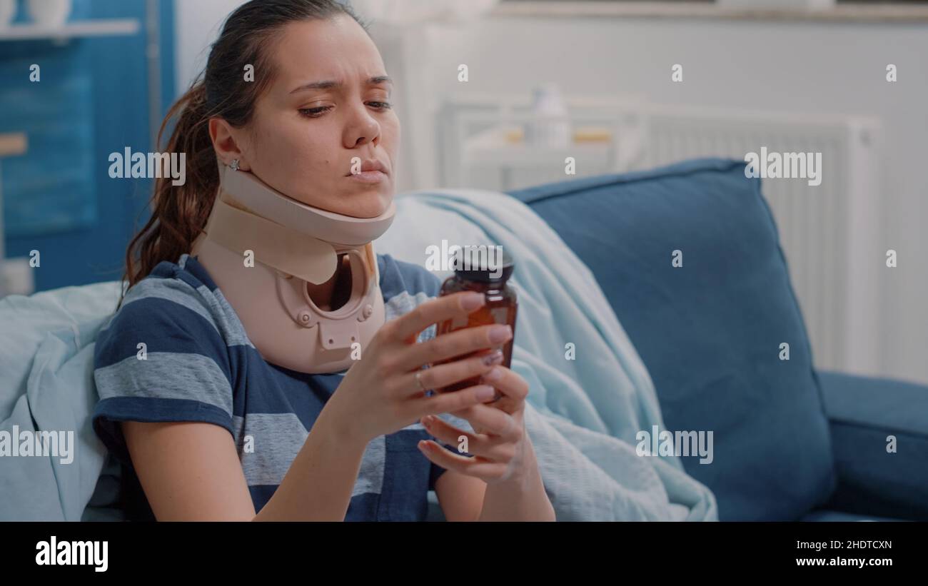 Woman with cervical neck foam looking at tablet and bottle of pills and ...