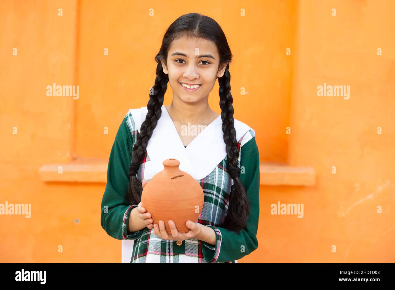 Portrait of happy Indian young girl holidng clay money box or gullak in ...