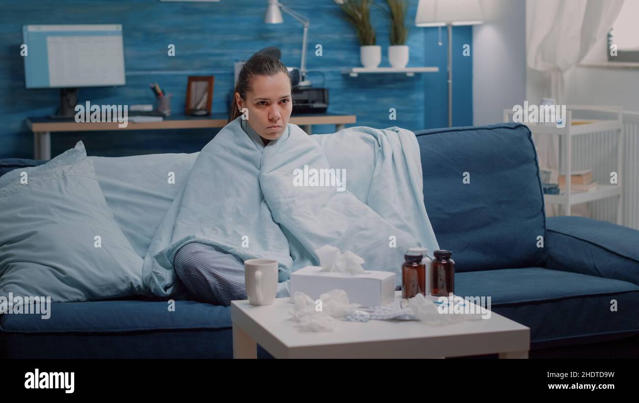 Sick woman with cold and flu sitting wrapped in blanket. Unhappy adult ...