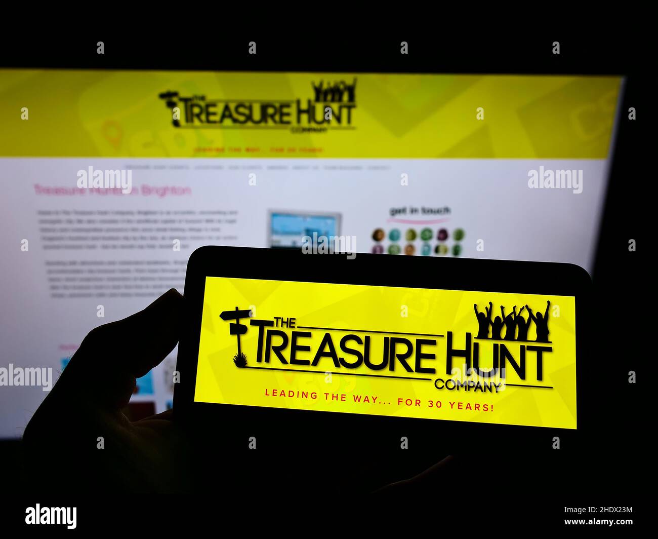 Person holding mobile phone with logo of The Treasure Hunt Company ...