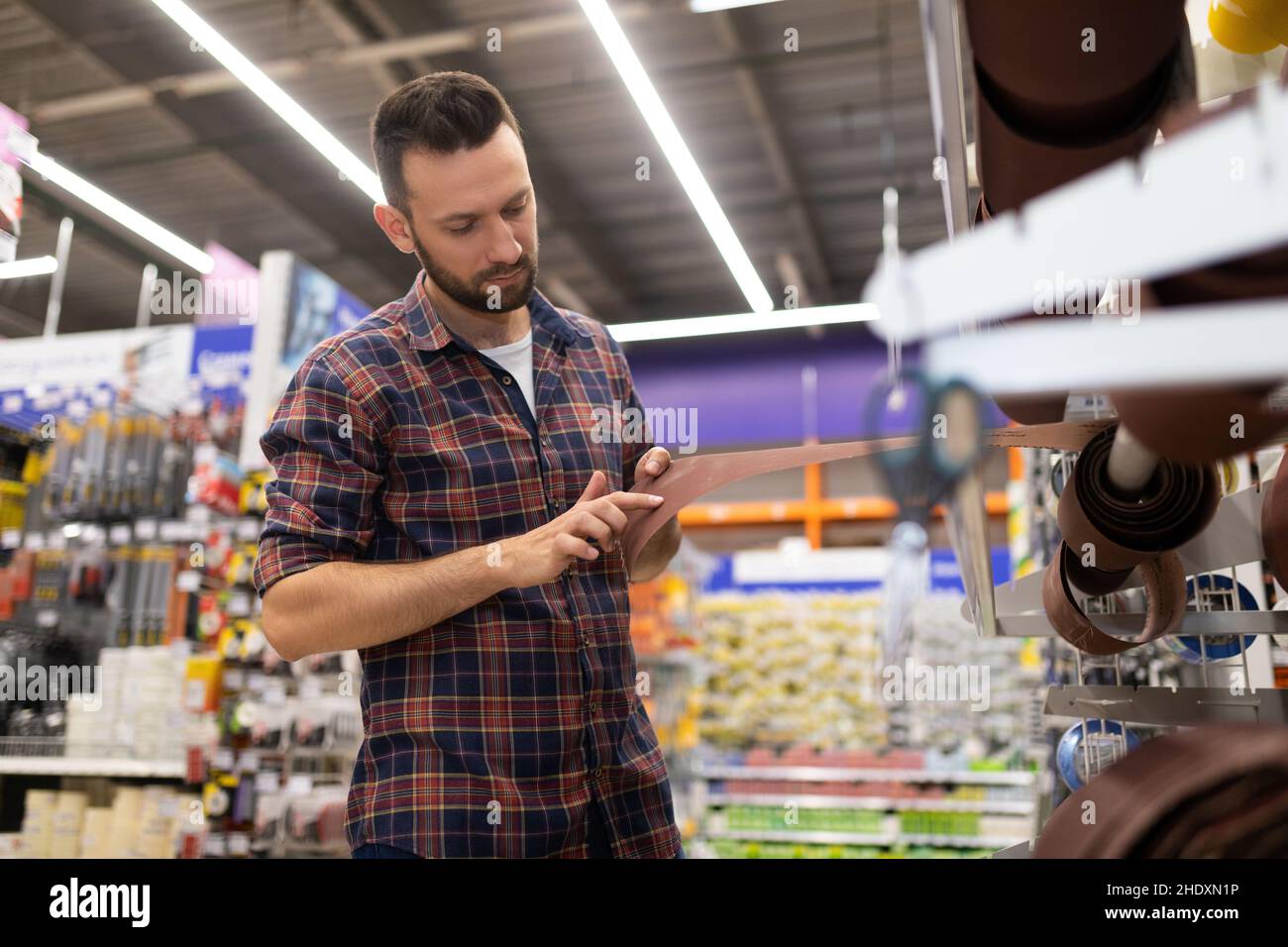 male buyer in a hardware store next to a rack with sandpaper for ...