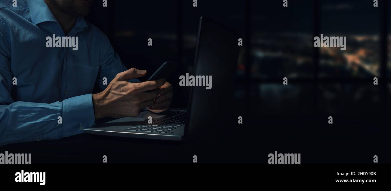 man working in dark office at night. using mobile phone and laptop ...
