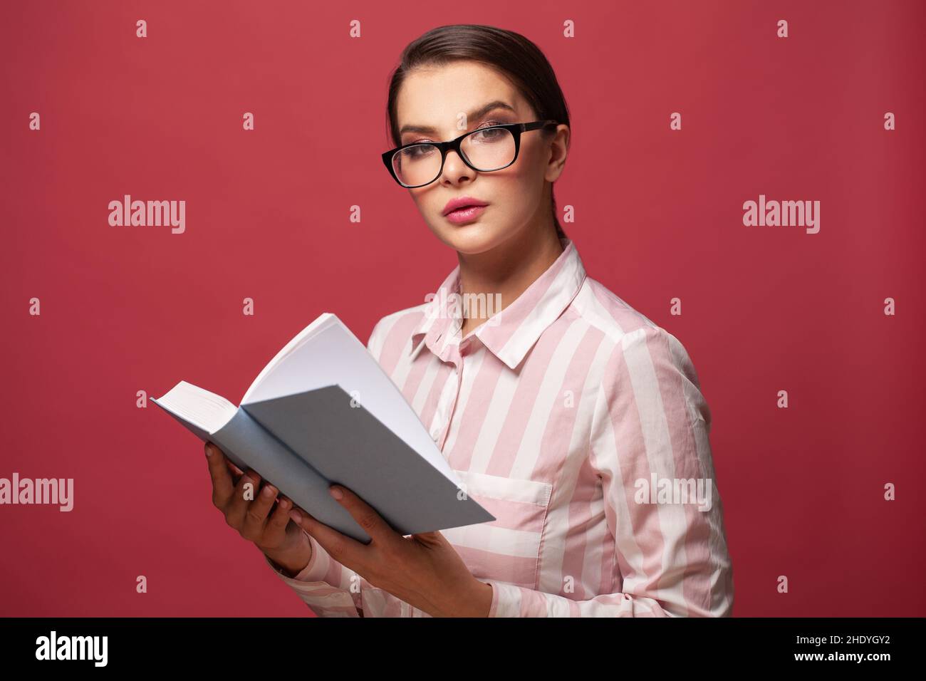 Cute woman in glasses reading a book on red, studio portrait Stock ...