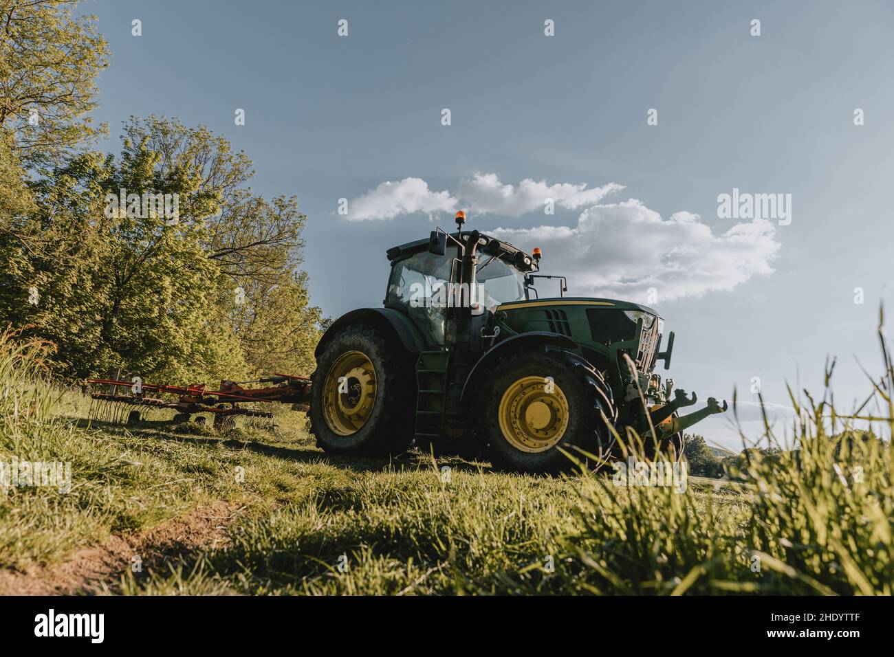 Low angle view of green tractor tedding the hay during the sunny may ...